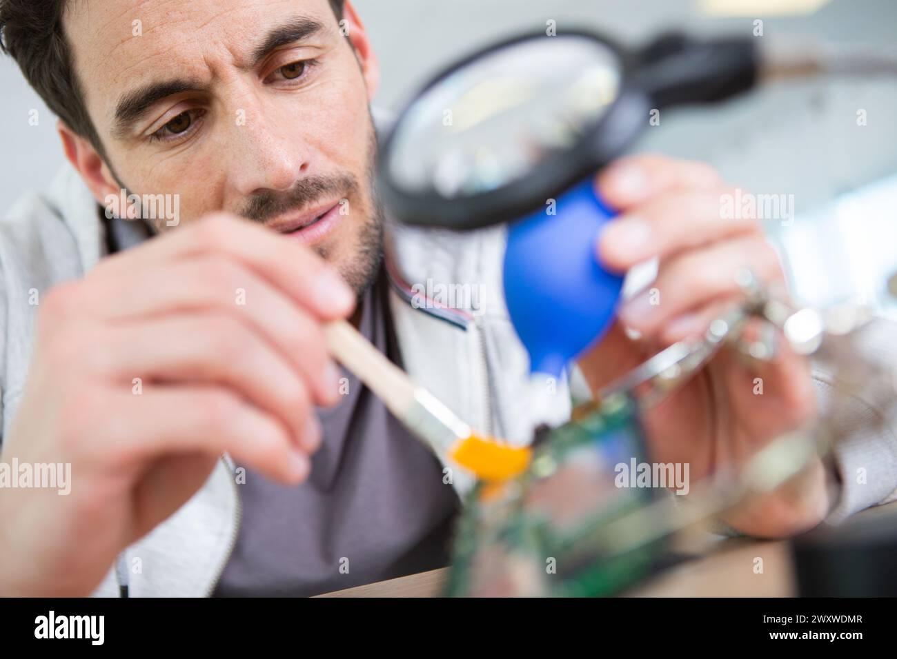 man working carefully with paint brush under magnifying glass Stock ...