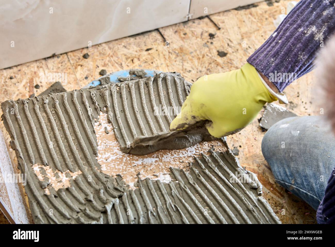 Applying adhesive cement mortar to back side of tiles using comb trowel ...