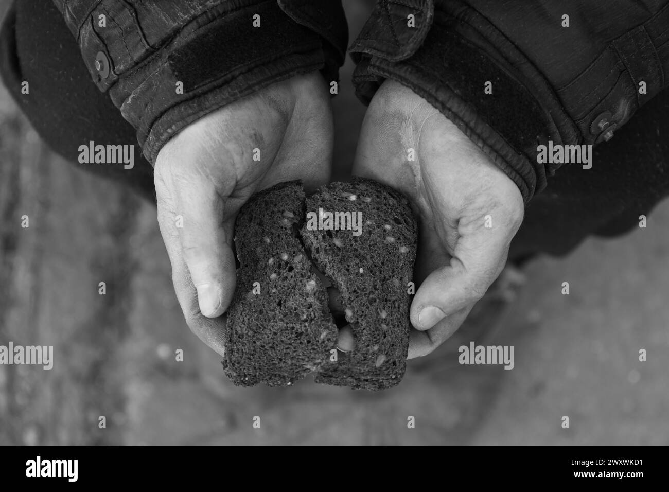 Poor homeless man holding piece of bread outdoors, top view. Black and ...