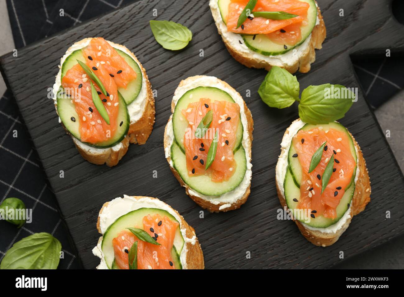 Tasty canapes with salmon, cucumber and cream cheese on grey table, top ...