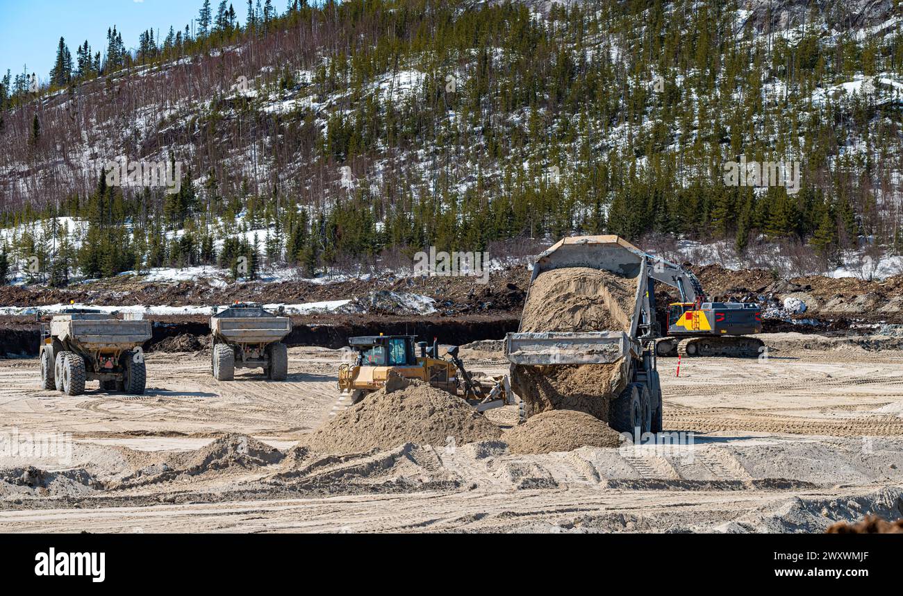 Three dump trucks with a bulldozer and an excavator on a construction ...