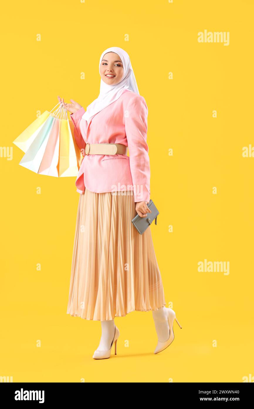 Beautiful young Muslim woman with shopping bags and purse on orange ...