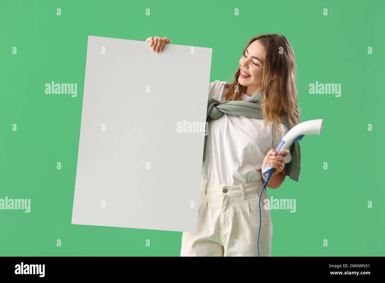 Pretty young woman with modern garment steamer and blank poster on ...
