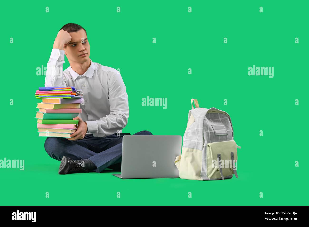 Stressed male student with stack of books and laptop on green ...
