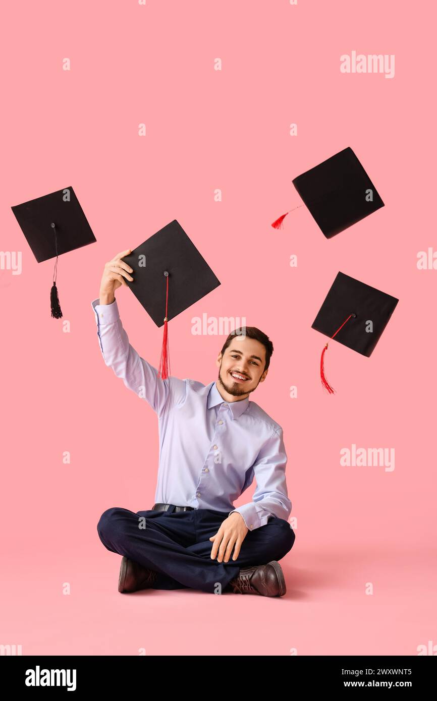 Male graduate student throwing mortar board up on pink background Stock ...