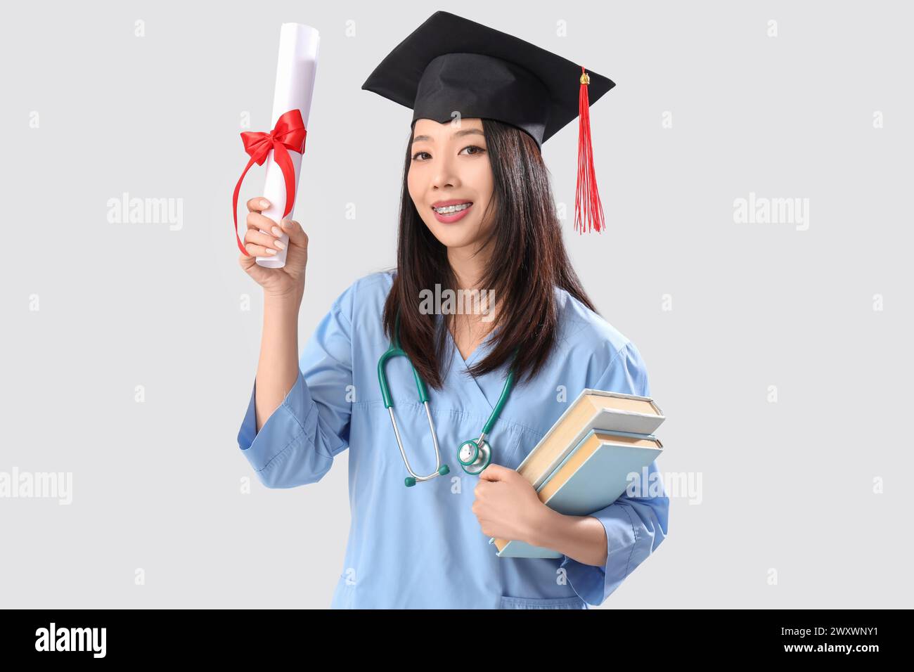 Asian female medical graduate student with diploma and books on white ...