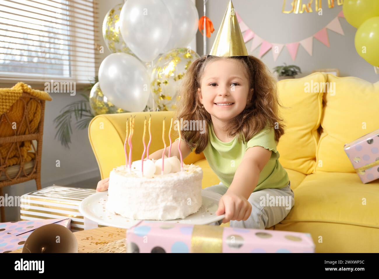 Cute little girl sitting on sofa in party hat with balloons, cake and ...