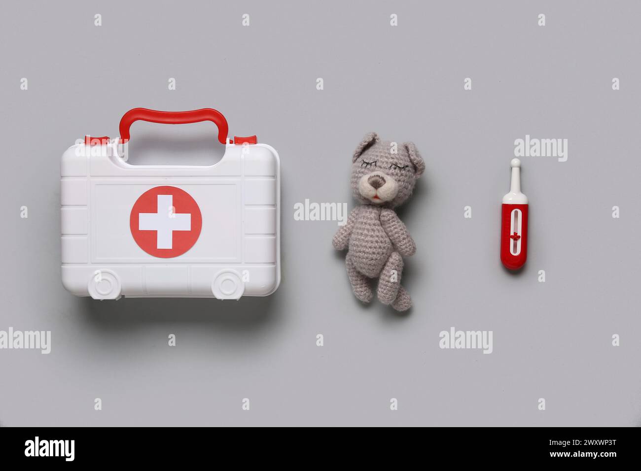 Toy first aid kit with teddy bear and thermometer on grey background ...