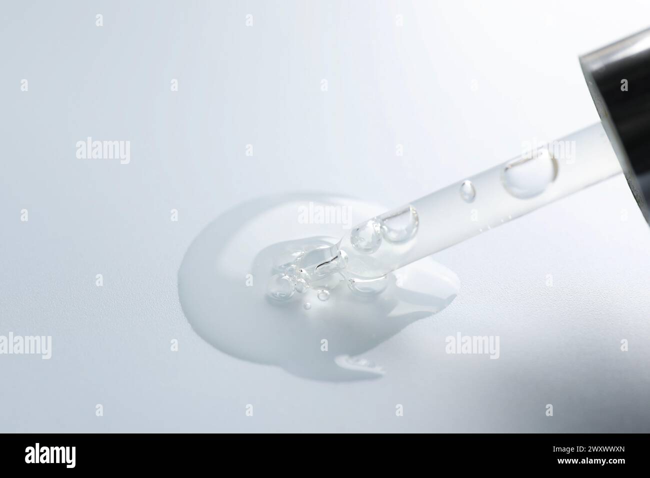 Dripping moisturizing serum from pipette on light grey background ...