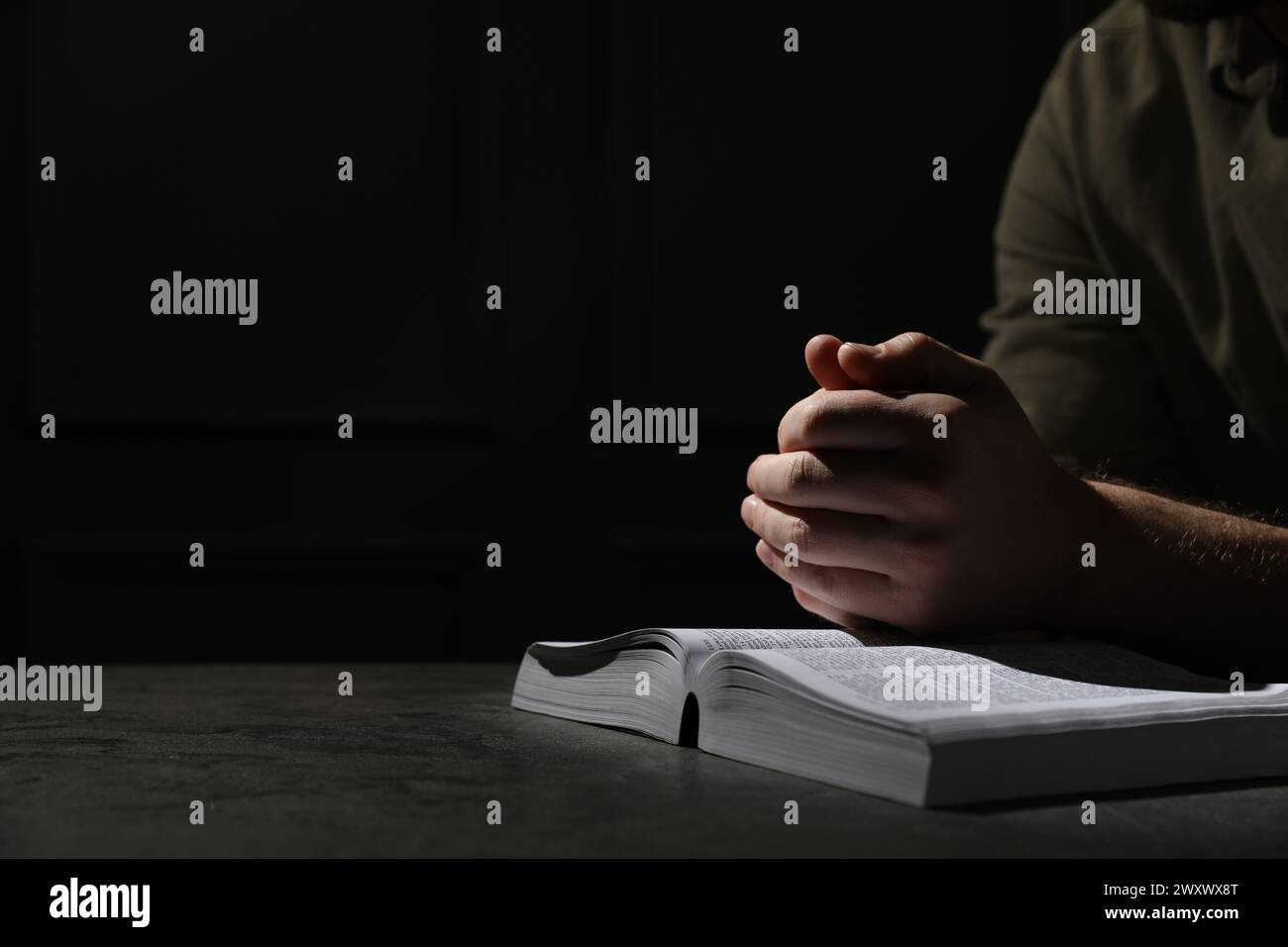 Religion. Christian man praying over Bible at table against black ...
