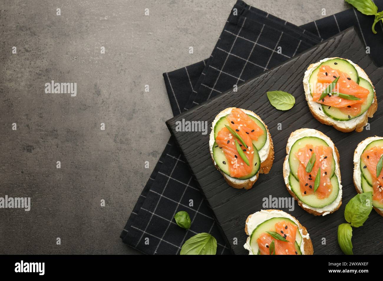 Tasty canapes with salmon, cucumber and cream cheese on grey table, top ...