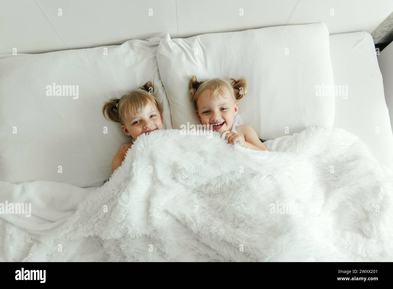 Two young female children are resting comfortably in a bed covered in ...