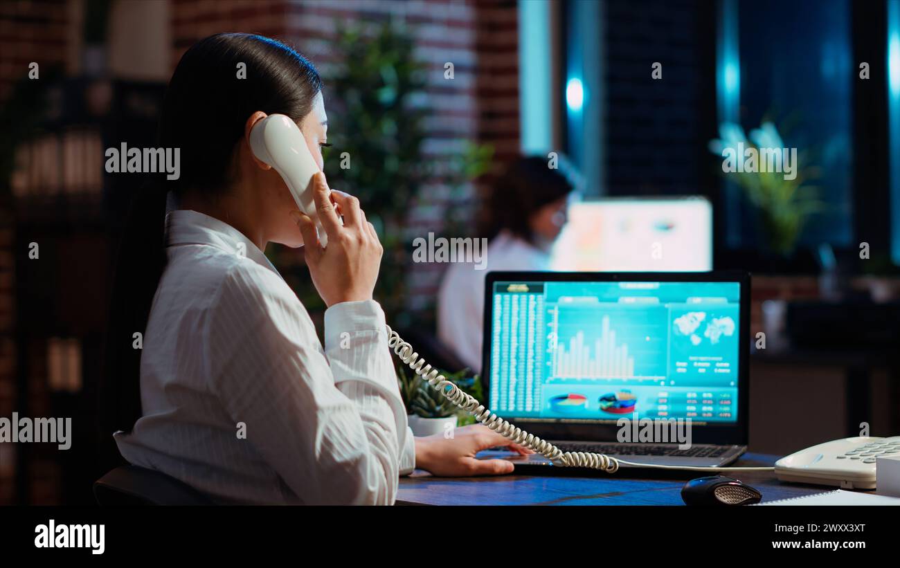 Asian employee taking landline telephone call while working with ...