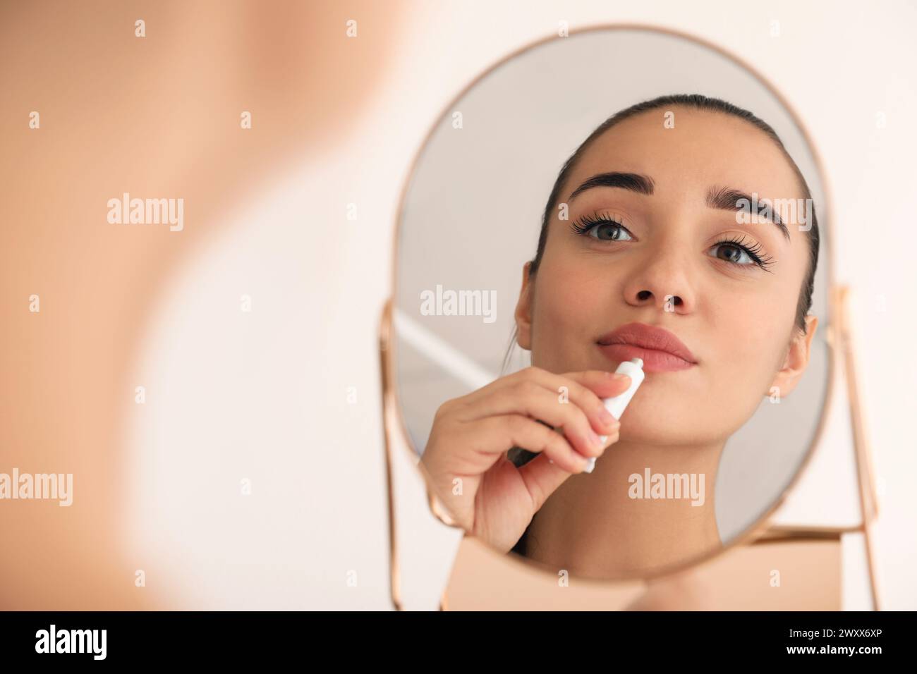 Woman with herpes applying cream on lips in front of mirror against ...
