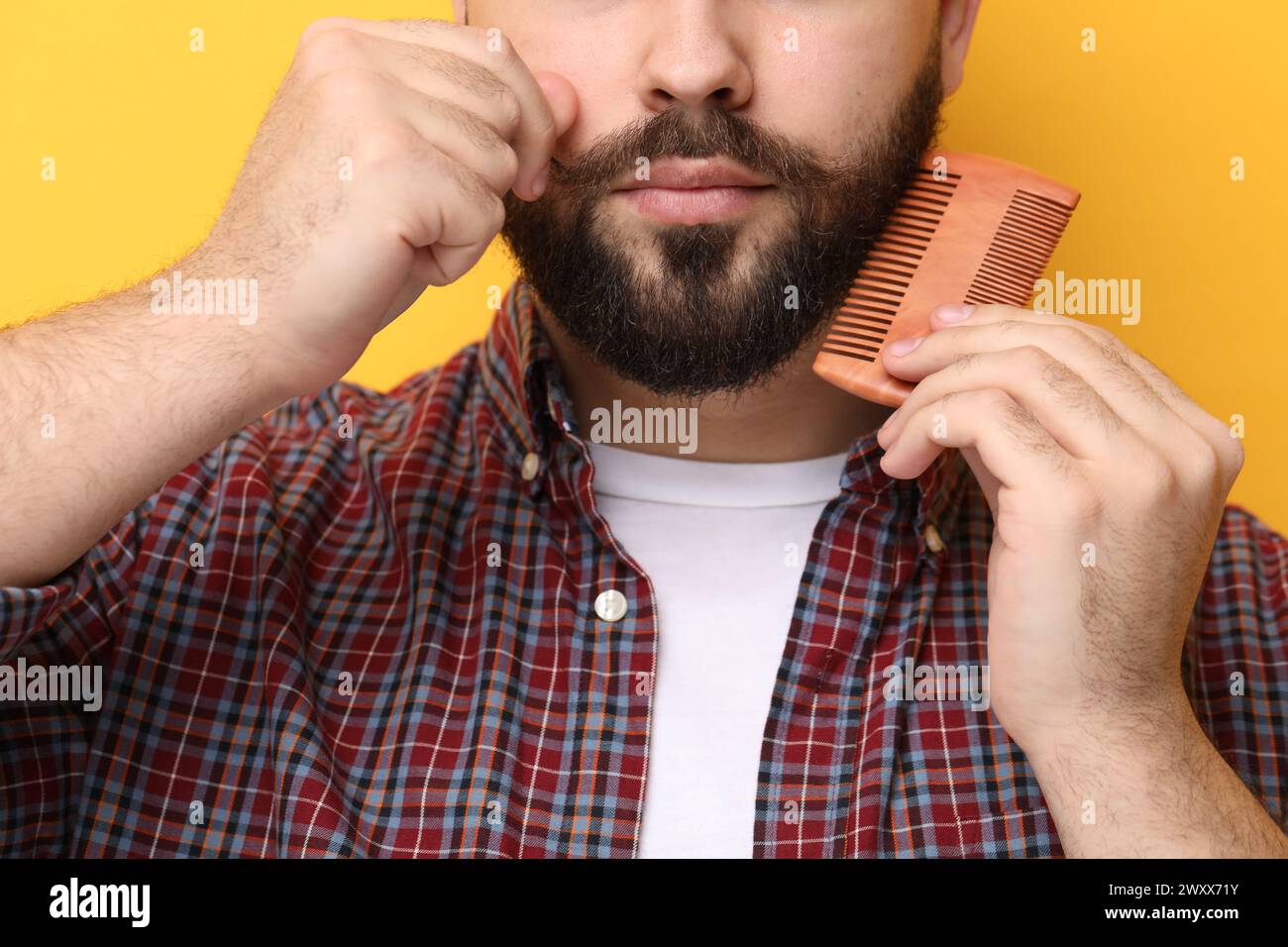 Handsome young man combing beard on yellow background, closeup Stock ...
