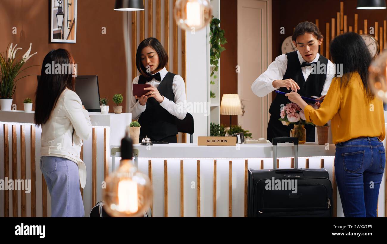 Tourists going through check in process at hotel reception desk, staff ...