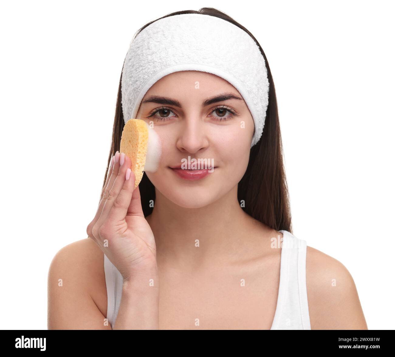 Young woman with headband washing her face using sponge on white ...