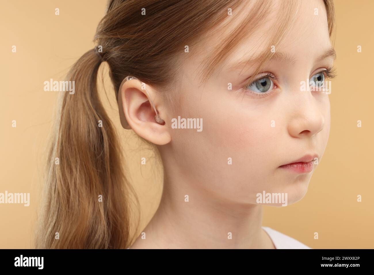 Little girl with hearing aid on pale brown background, closeup Stock ...