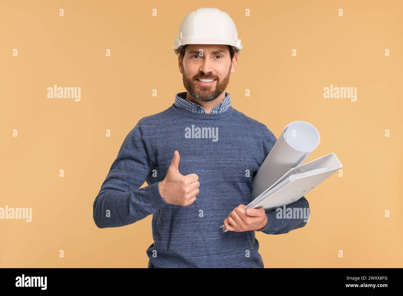 Architect in hard hat with draft and folder showing thumbs up on beige ...
