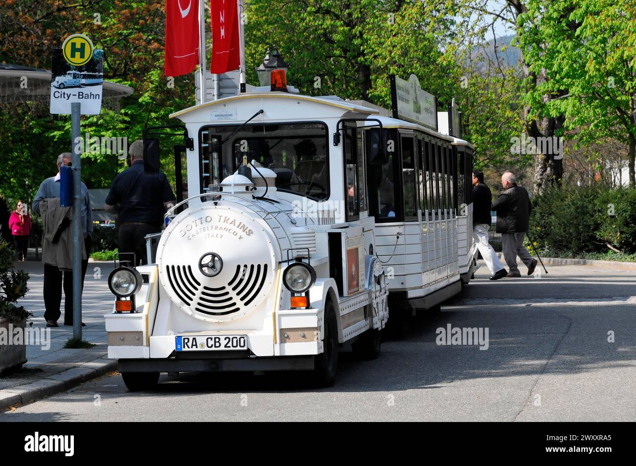 Spa garden, A white tourist train stops on a street while people get on ...