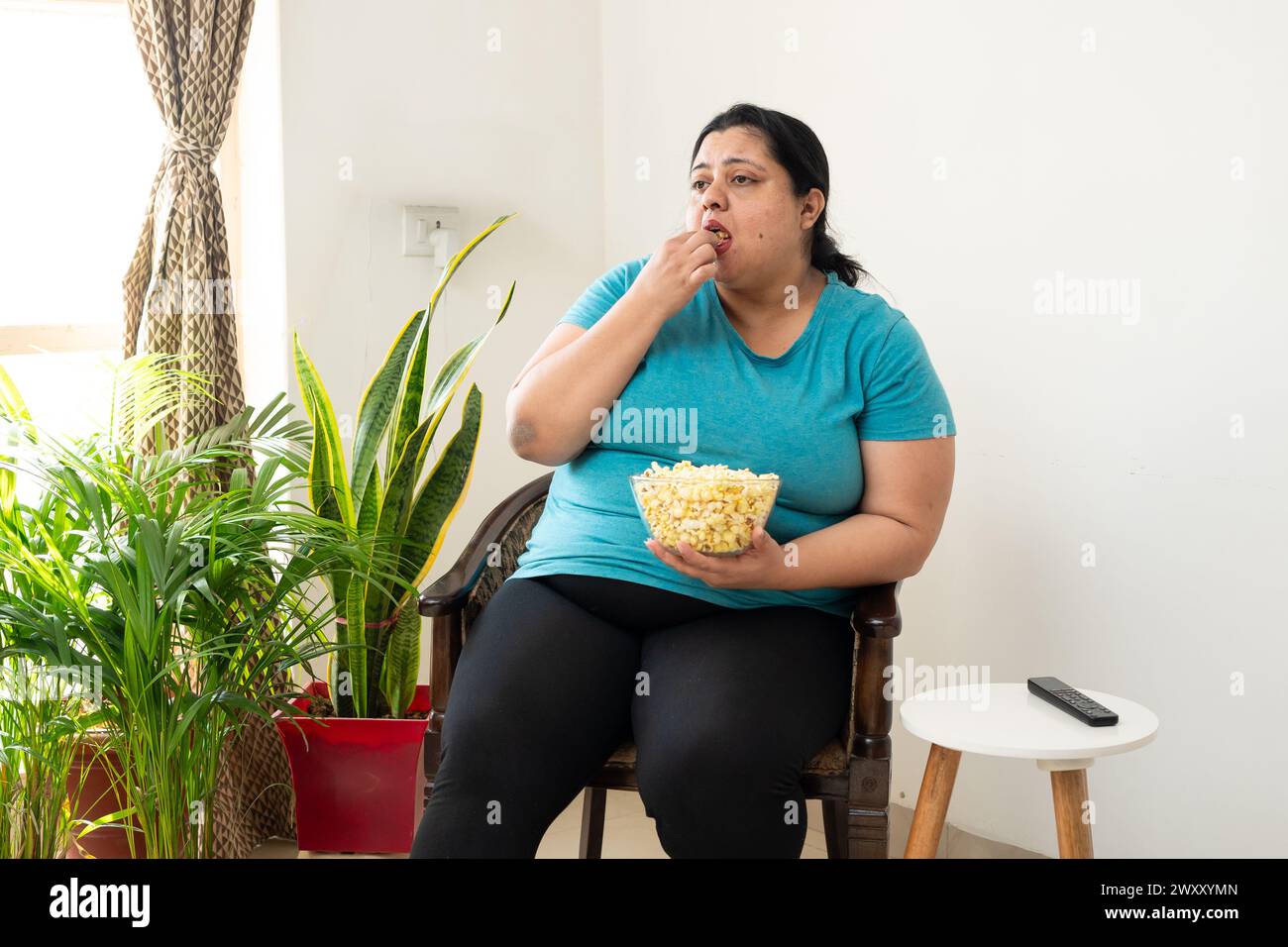 Overweight fat indian woman sitting on chair eating popcorn at home ...