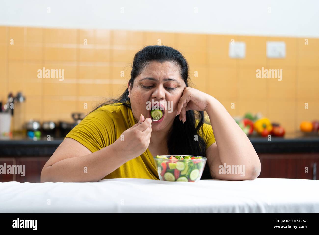 Sad Overweight fat indian woman holding fork and eating vegetable salad ...