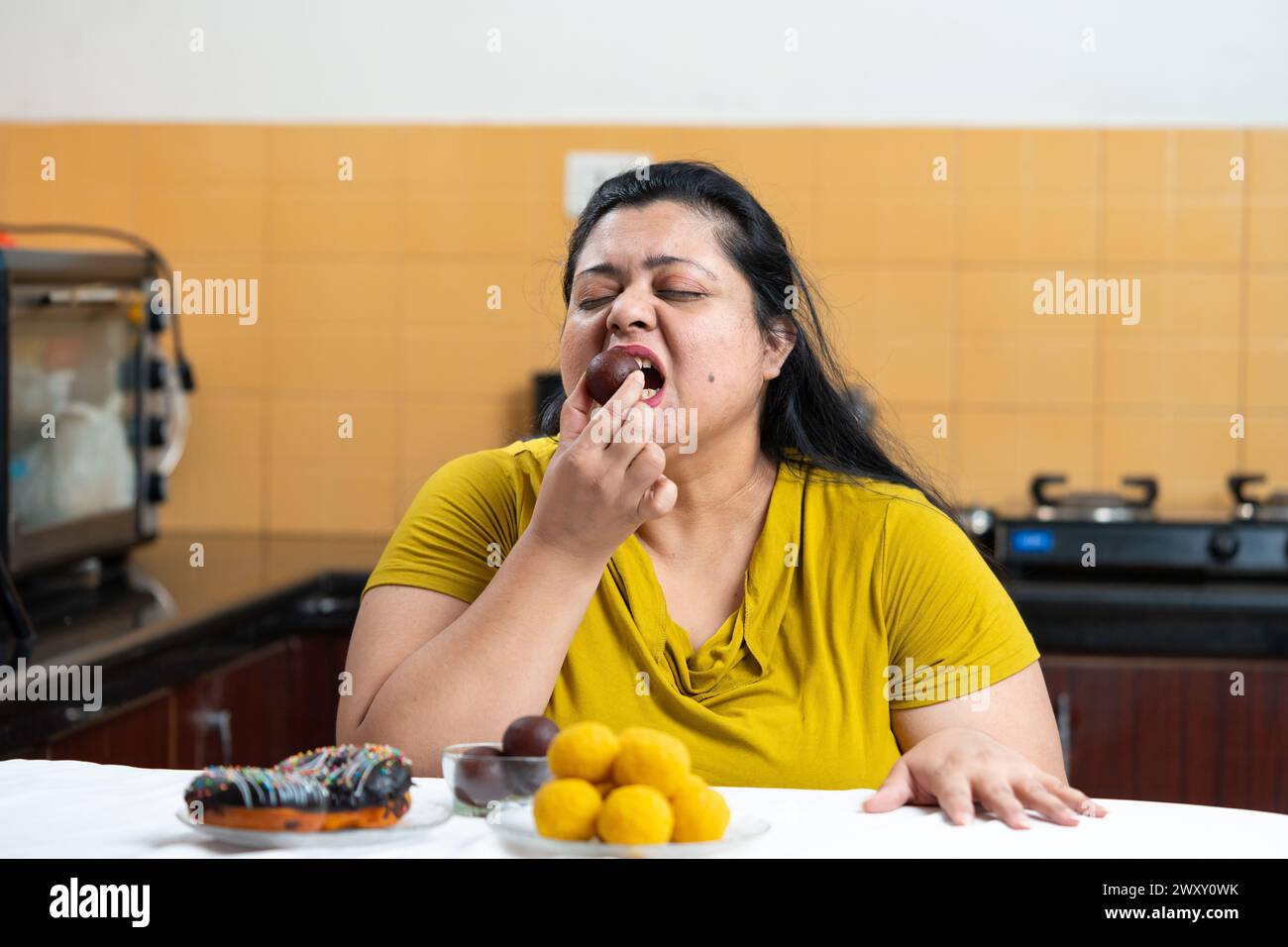 Overweight fat indian woman eating gulab jamun and donuts, laddu or ...