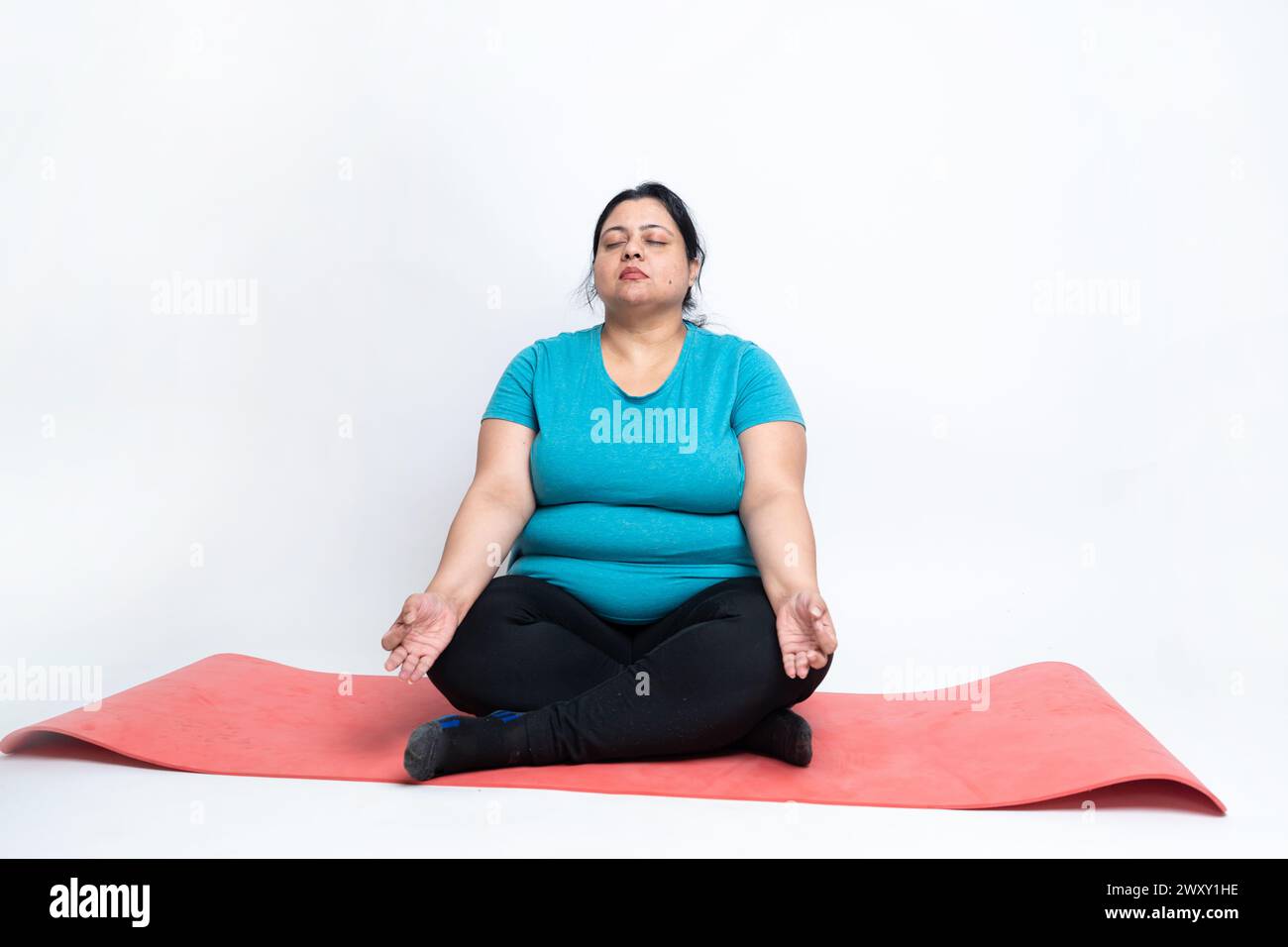 Overweight fat indian sitting on yoga mat doing yoga or meditation with ...