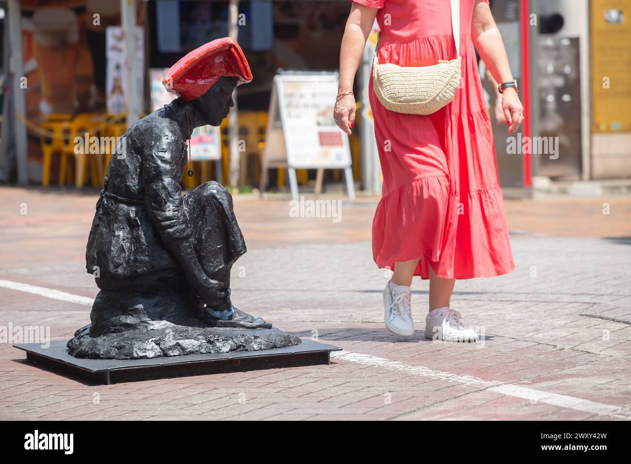 3 April 2024. A woman in long dress walks past a bronze Samsui woman ...