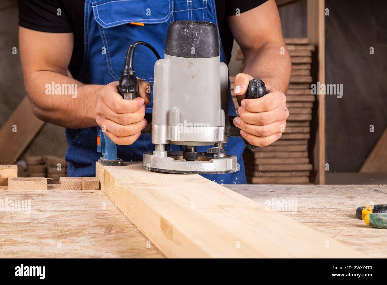Male carpenter using electric sander to polish wooden plank in joinery ...