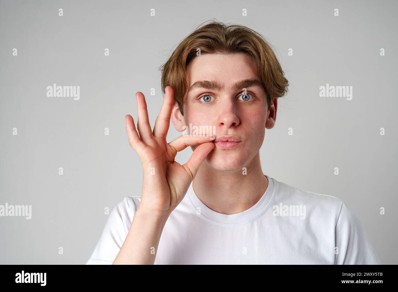 Young Man Performing Hand Gesture Near Face Against Plain Background ...