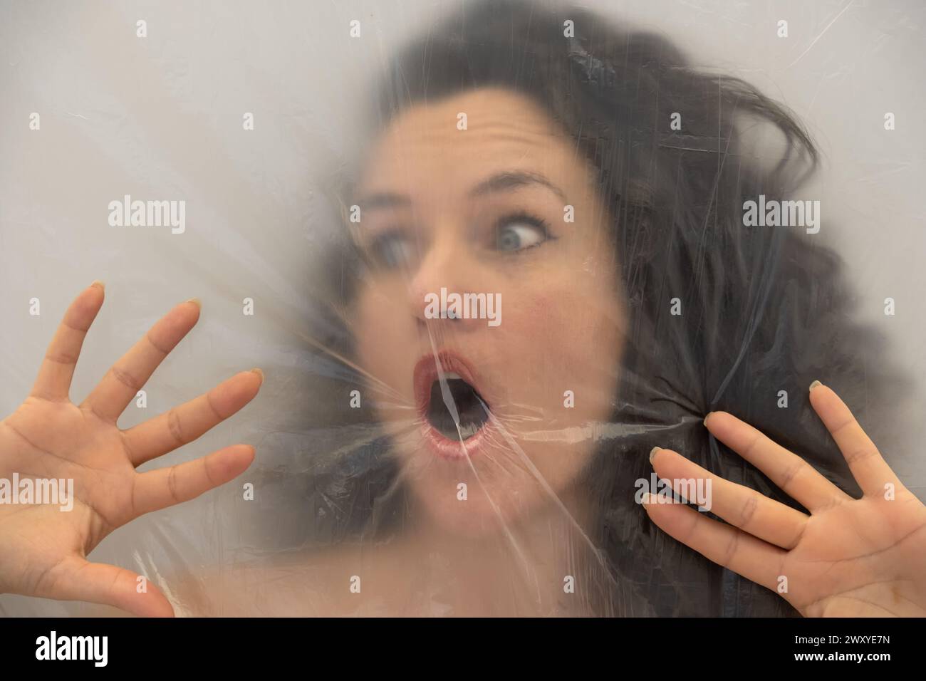 blurred portrait of a brunette curly woman behind transparent plastic foil with defensive hands ...