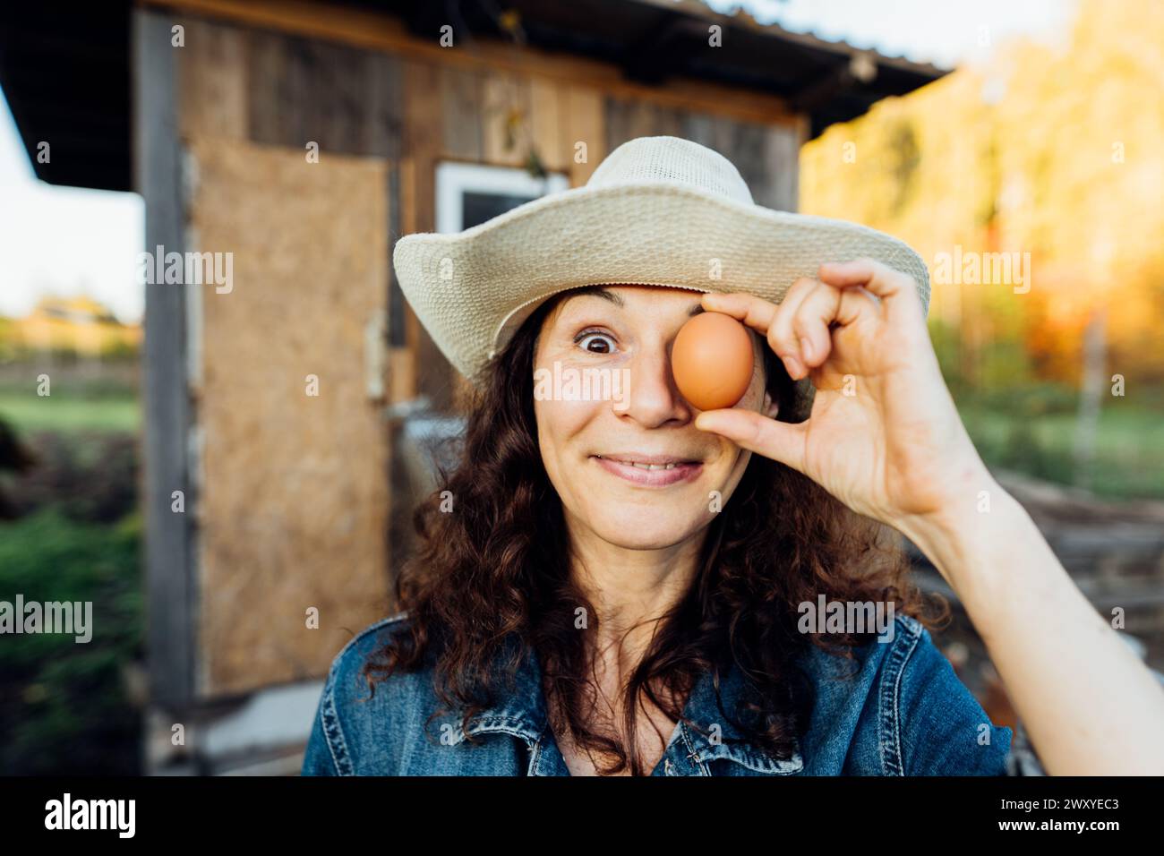 Laughing Woman in Hat Holds Egg to Face, Closing Eye Stock Photo - Alamy