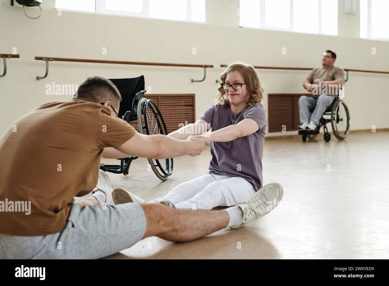 Joyful young woman with disability sitting on floor doing stretching ...