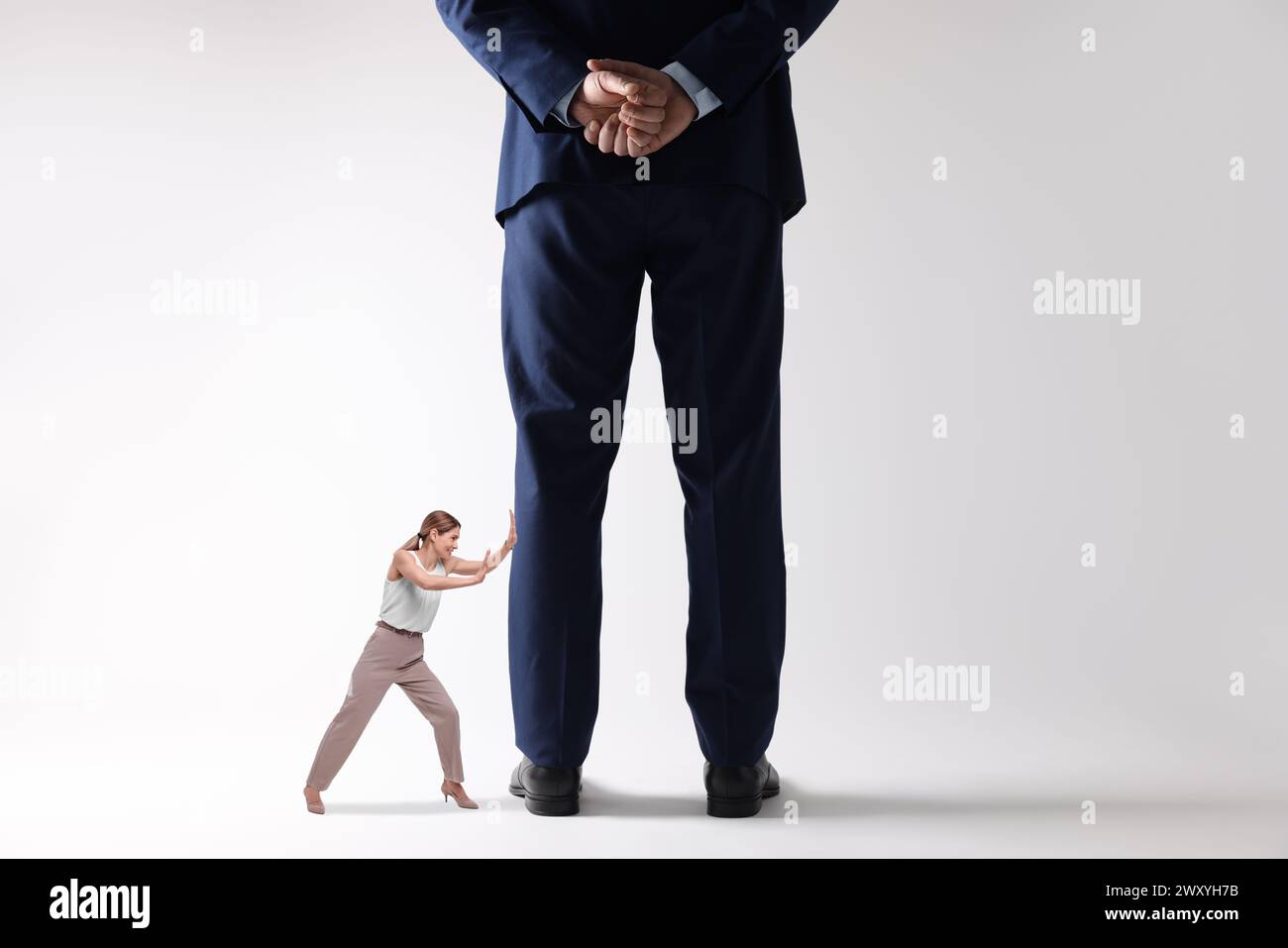 Small woman pushing giant man on light background Stock Photo - Alamy