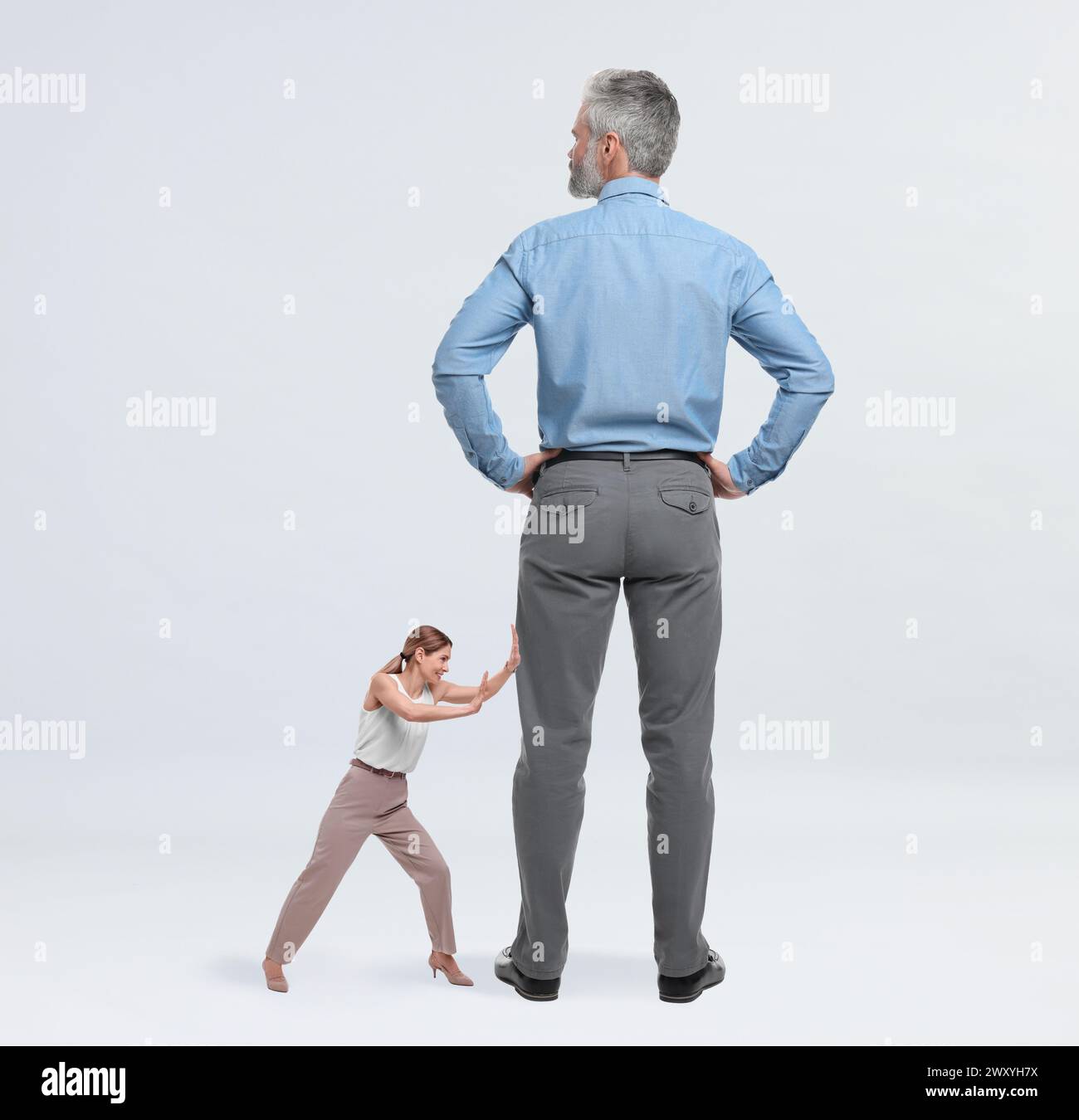 Small woman pushing giant man on light background Stock Photo - Alamy
