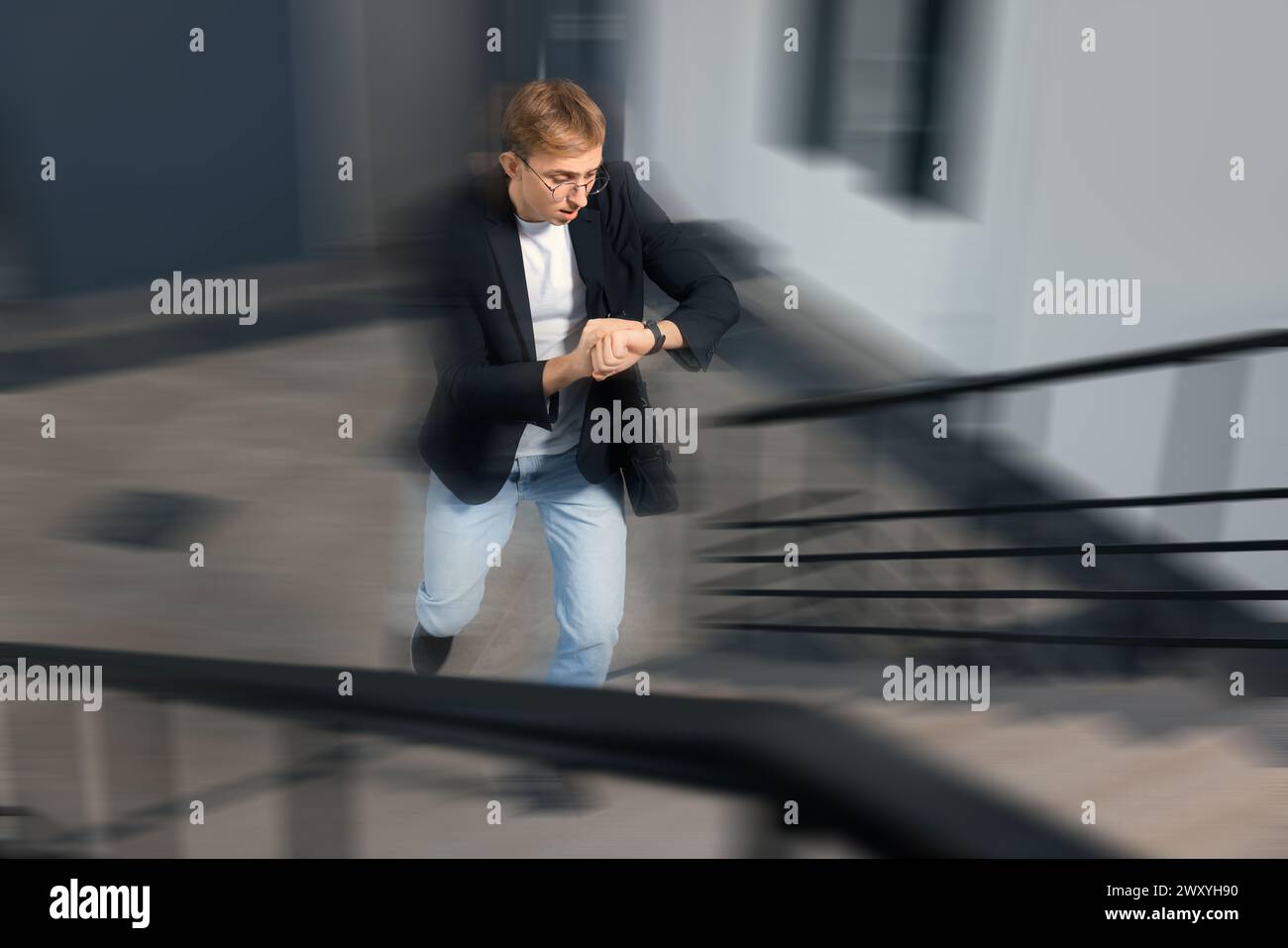 Being late. Young man checking time while running up stairs indoors ...