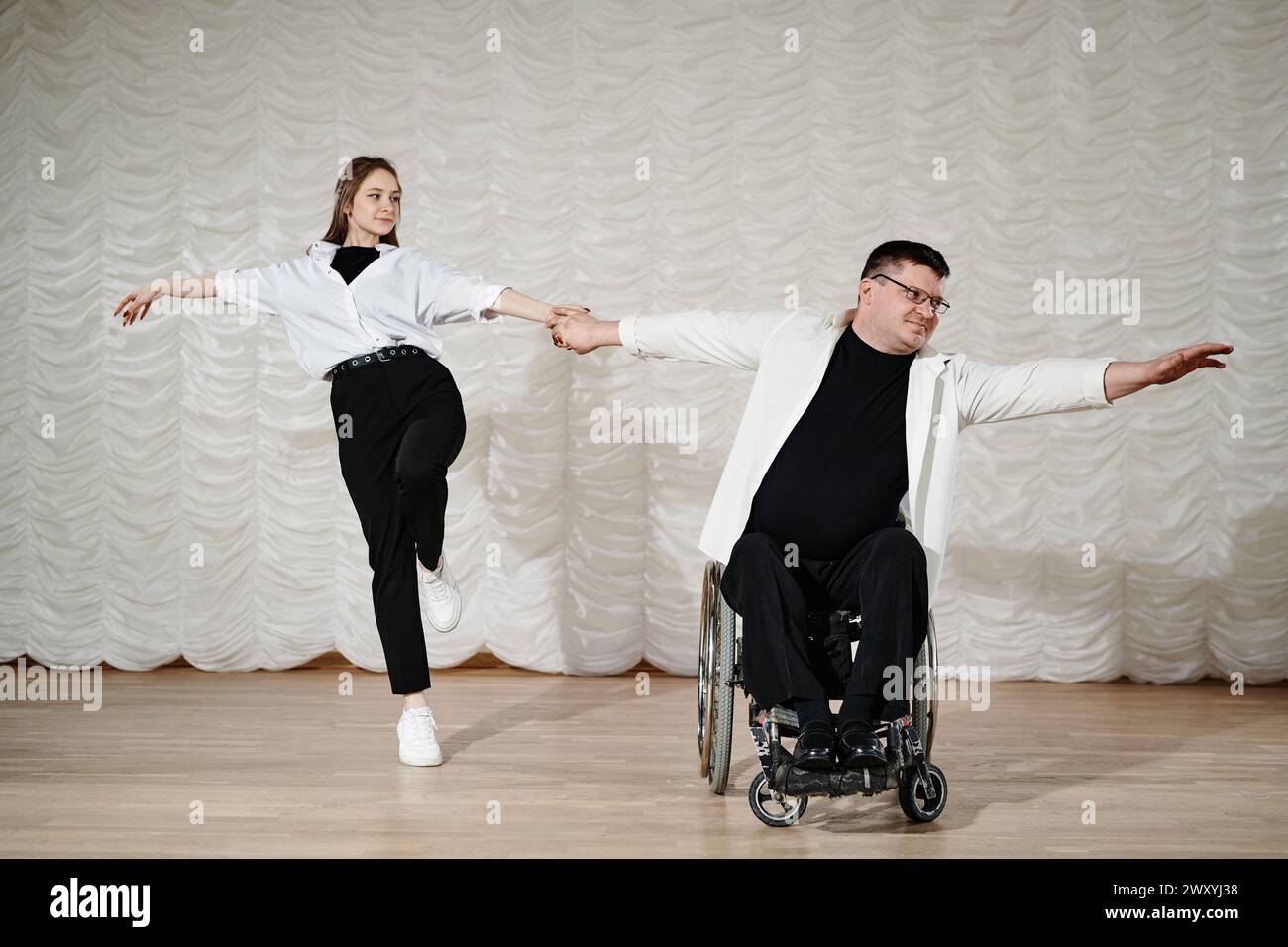 Long shot of young woman and mature man with disability in wheelchair ...