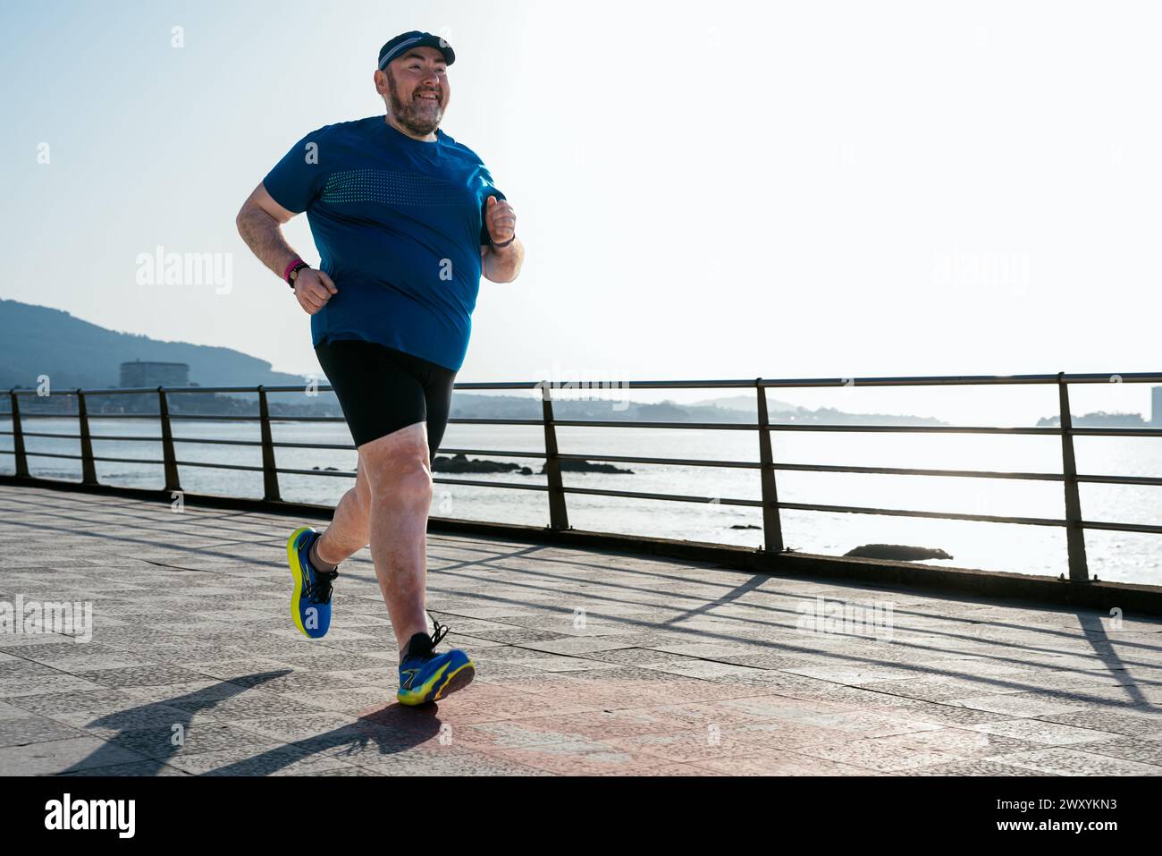 An active man in sportswear is jogging along a sunny seaside promenade ...