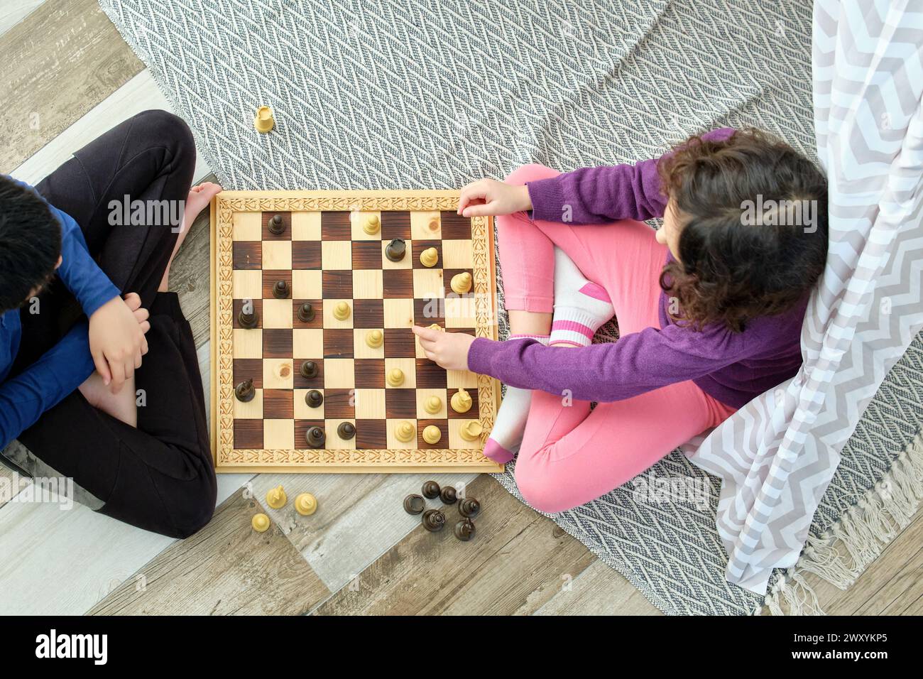An overhead view of a boy and a girl playing chess on a wooden board ...