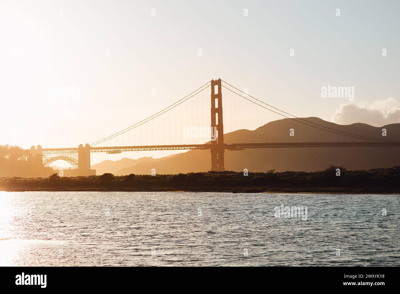 The setting sun casts a golden silhouette of the Golden Gate Bridge ...