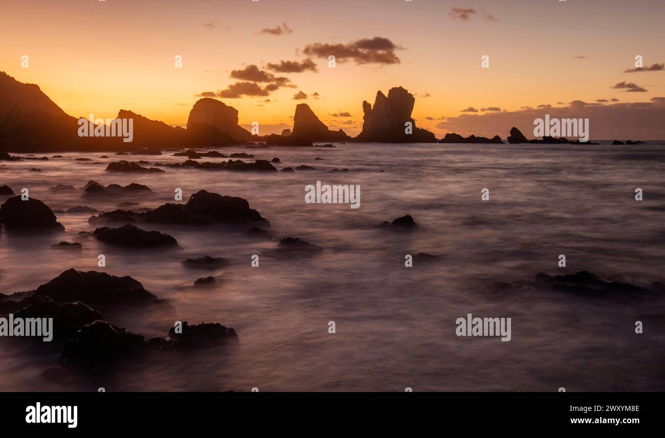 The golden hues of sunset bathe the sky as the silhouettes of rugged ...