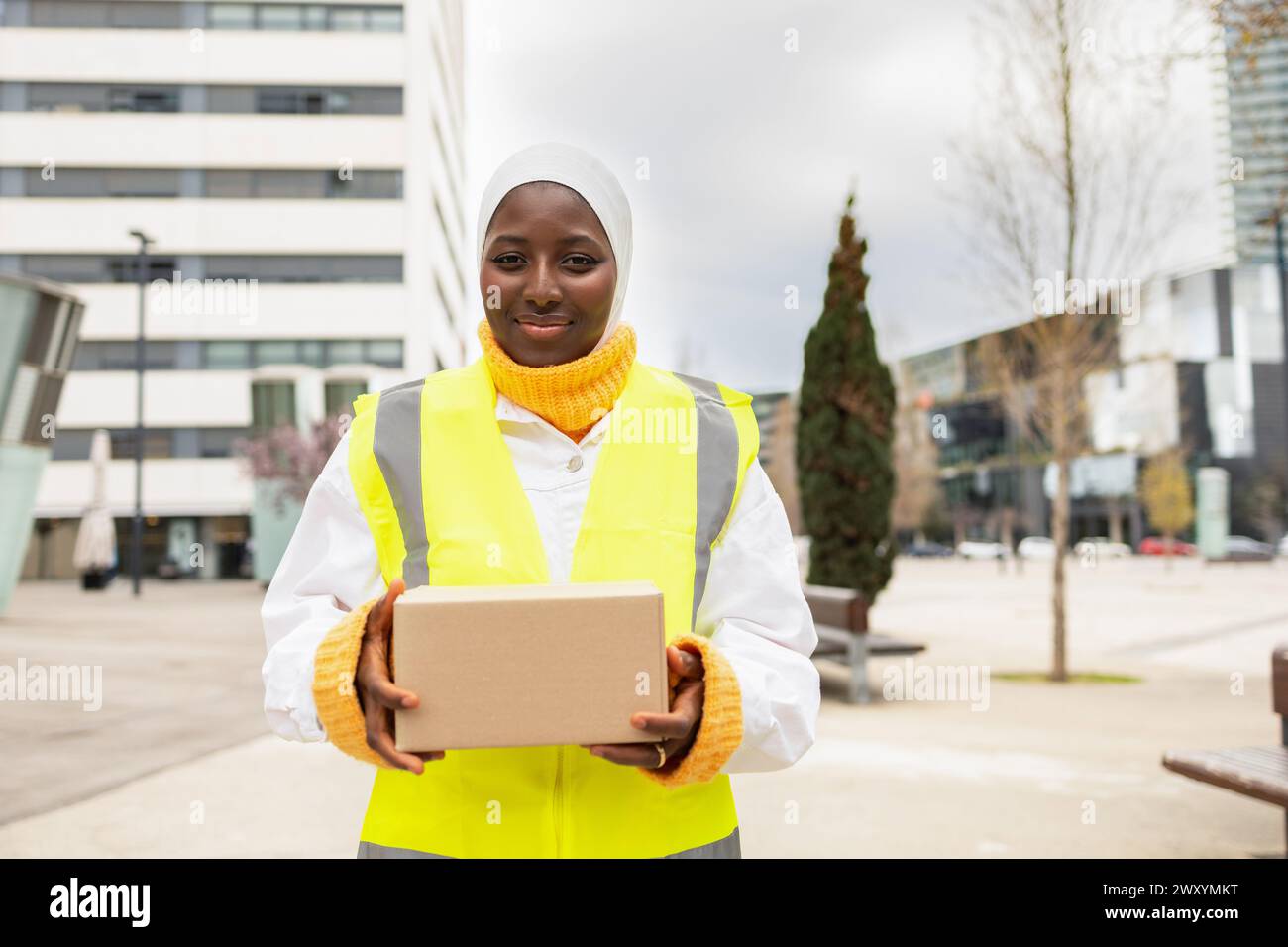 A confident African american woman in a hijab and safety vest holding a ...