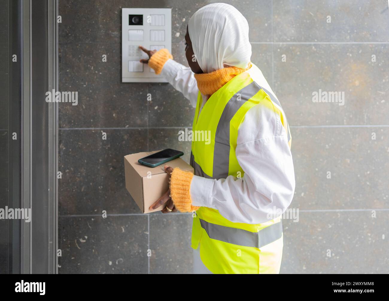 Side view of woman in a safety vest, hijab, delivering a package and ...