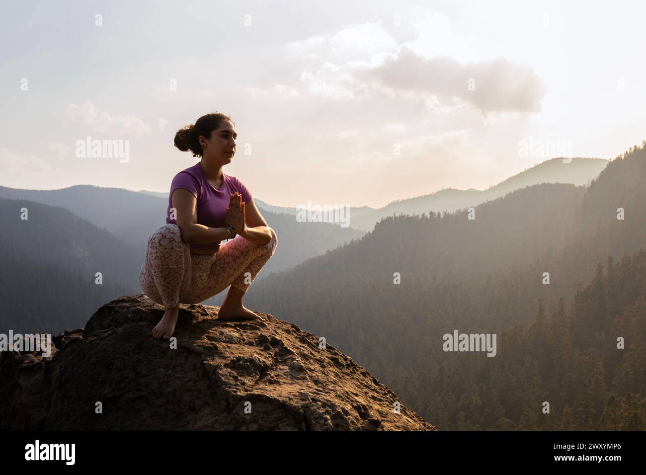Captured at dusk, a yogi squats in a pose of reflection on a high rock ...