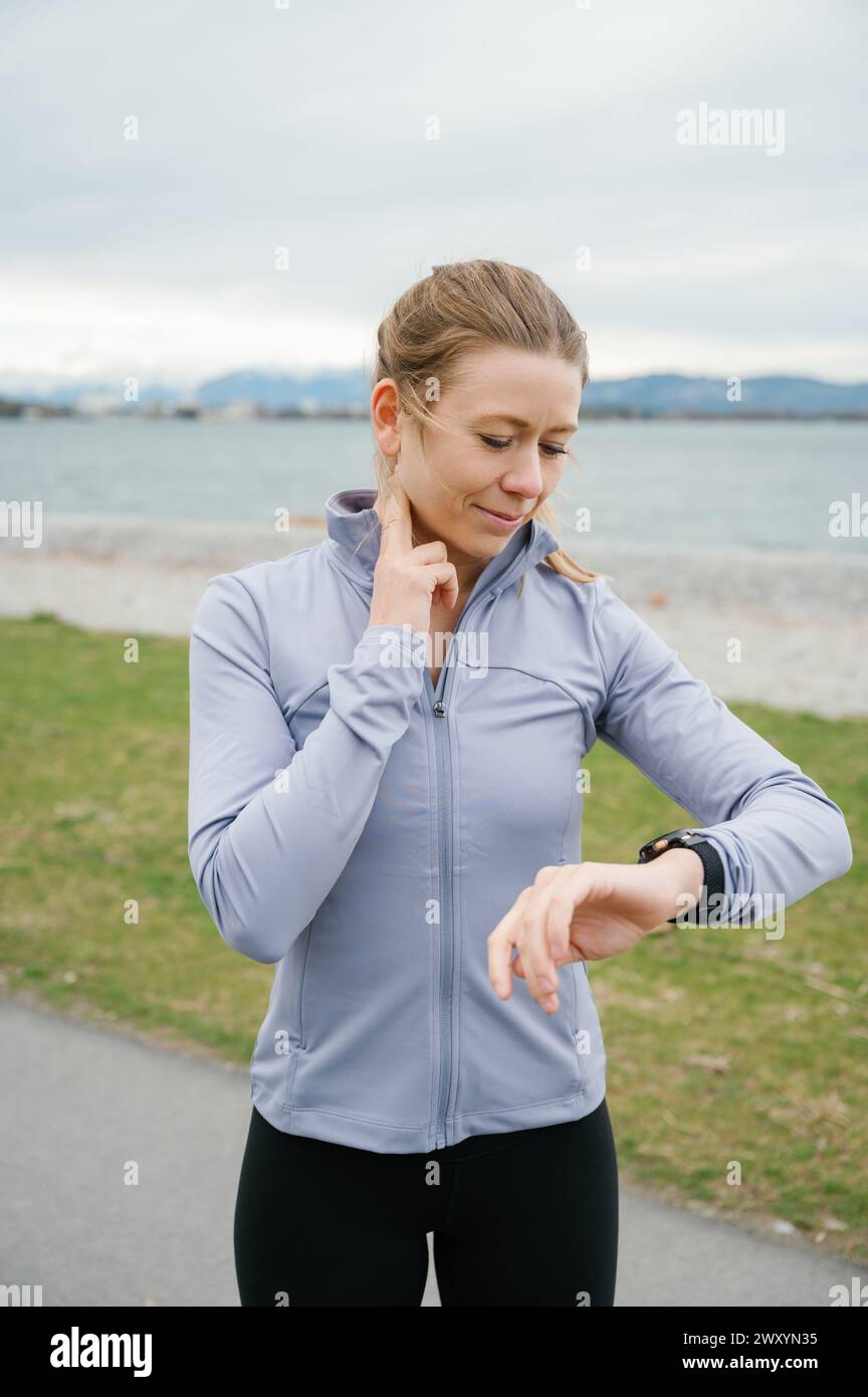 A focused female runner pauses to check her smartwatch or fitness ...