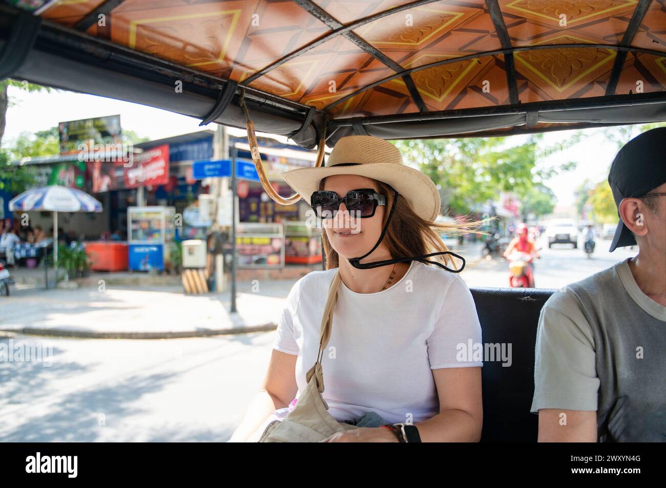 A young female tourist wearing a hat enjoys a tuk-tuk journey through ...