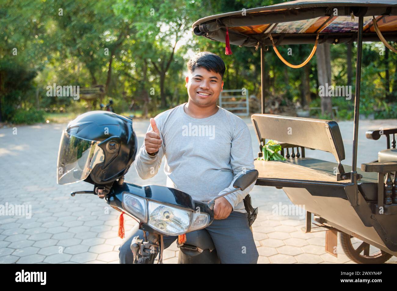 A cheerful man poses with a tuk-tuk, giving a thumbs-up signal next to ...