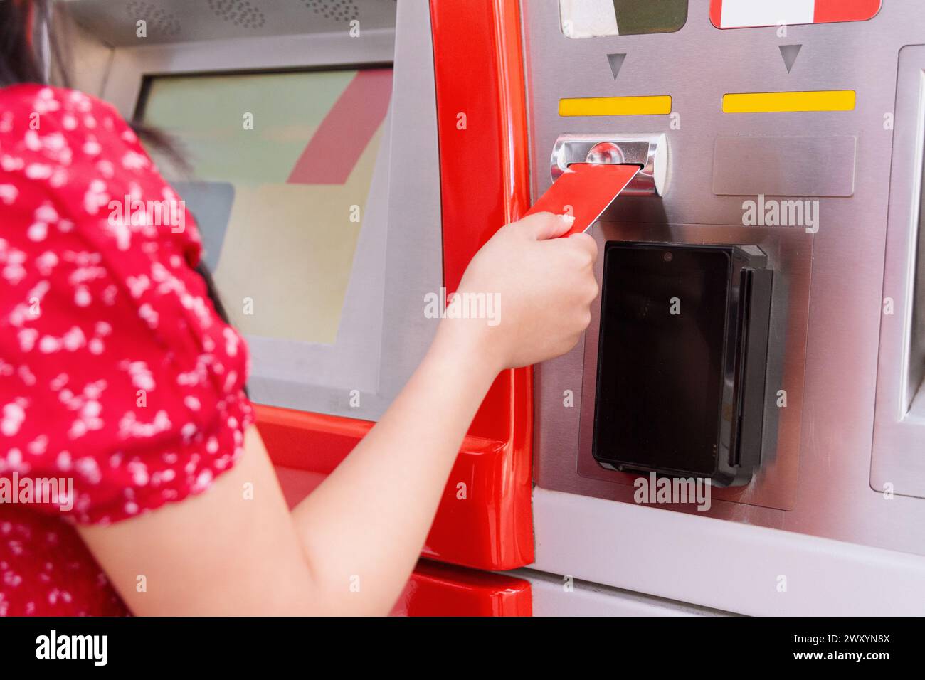 Close-up view of a woman's hand inserting a red debit card into an automated teller machine ...