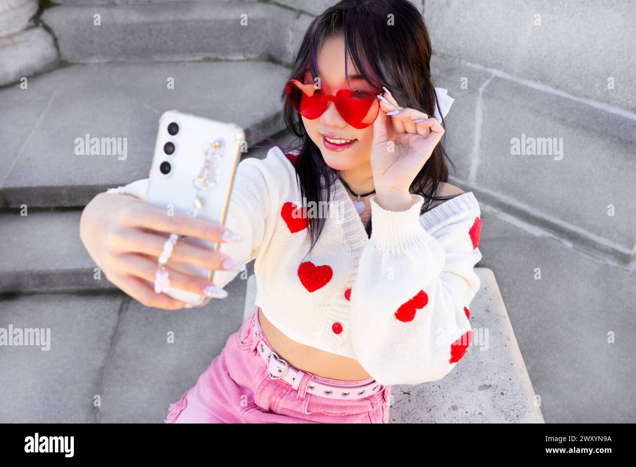 A fashionable Gen-Z chinese girl poses with a smartphone, taking a ...